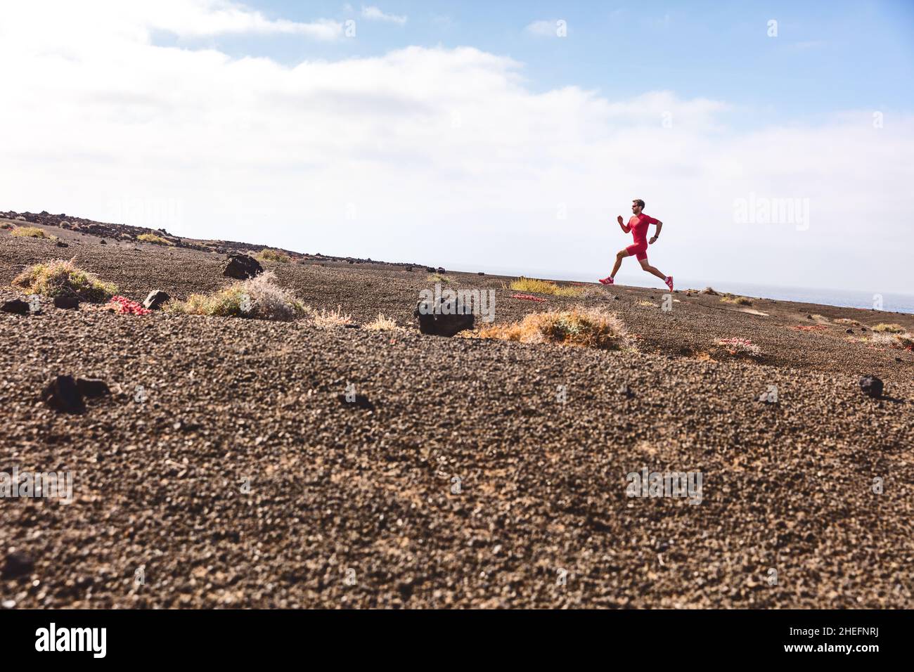 Trail runner athlete ultra running uphill on volcanic rock mountain ...