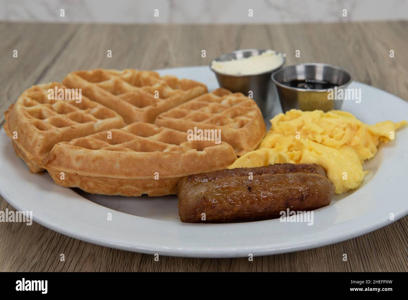 Round waffle for tradional breakfast with sausage, eggs, syrup, and ...