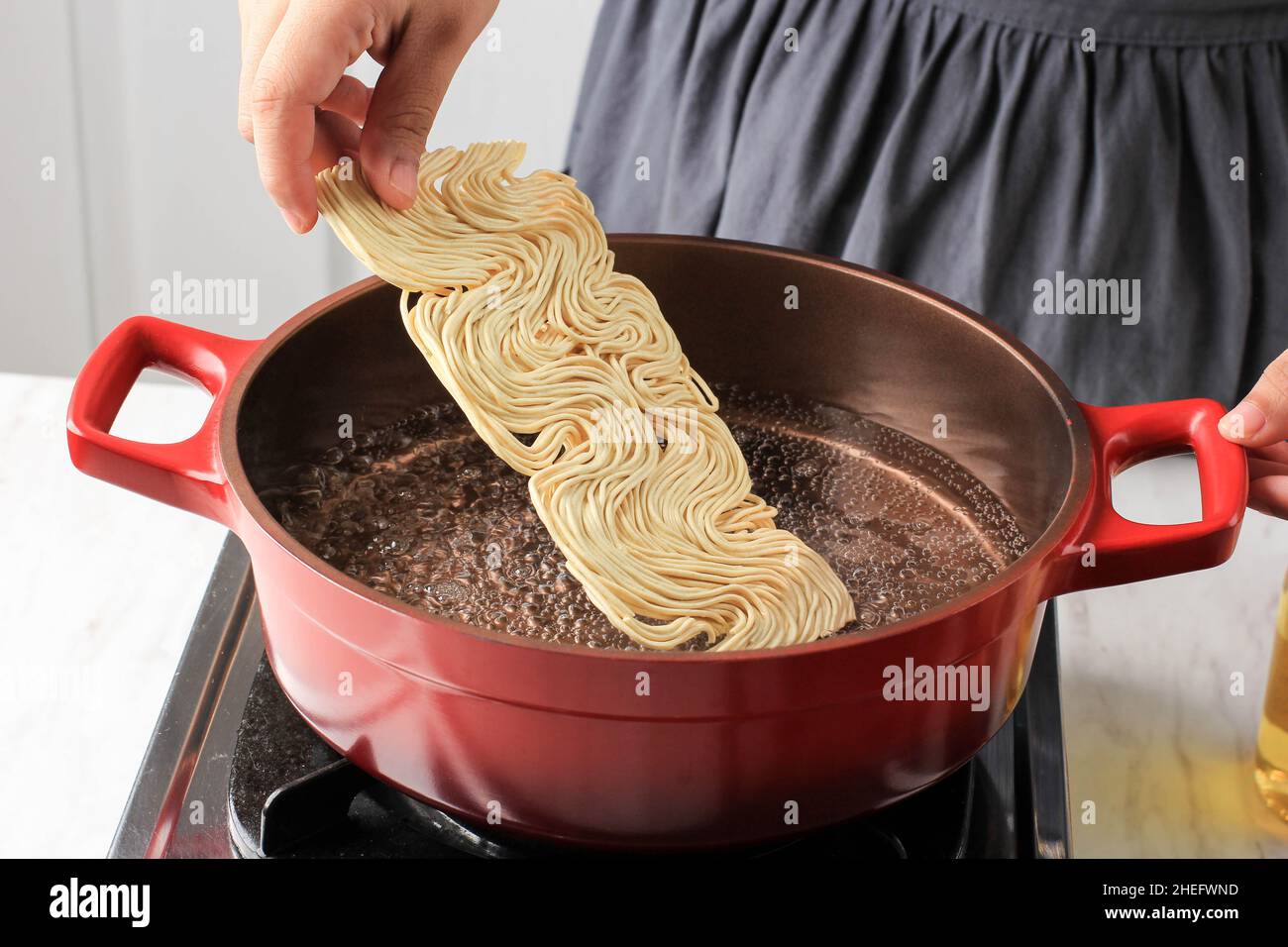 Female hand Put Dry Asian Egg Noodle to the Boiled Water in a Red Pan ...