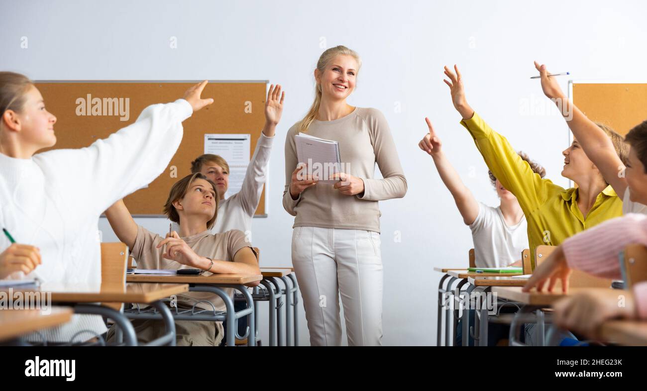 Female teacher lecturing in classroom and kids raising hands Stock ...