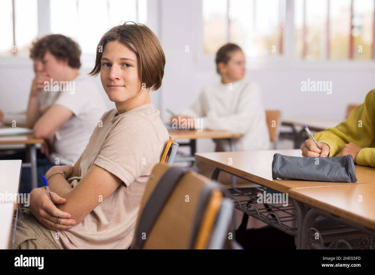Brooding boy stands in a school class against background of classmates ...