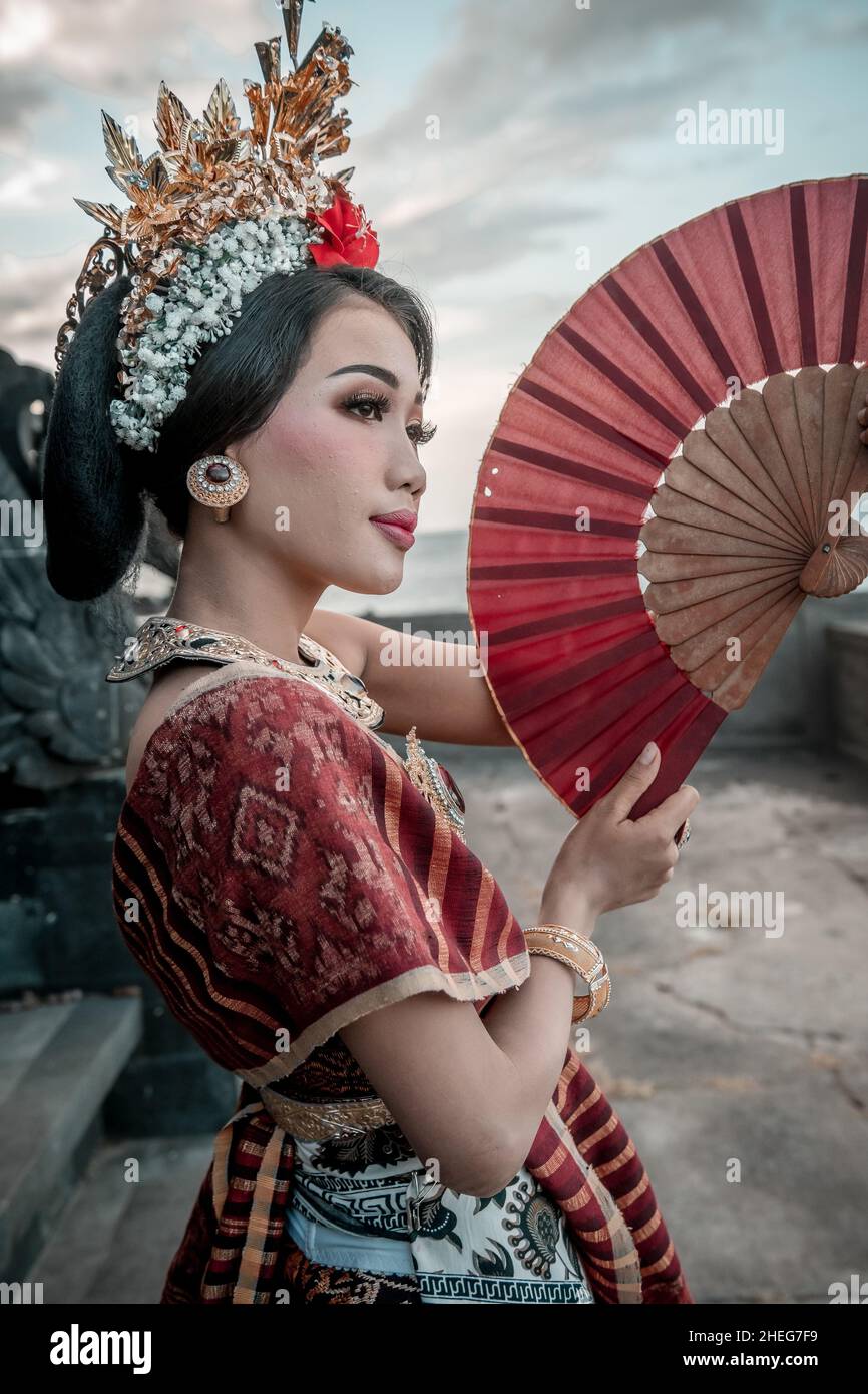 Portrait Bali girl with a traditional dress standing with folding fan ...