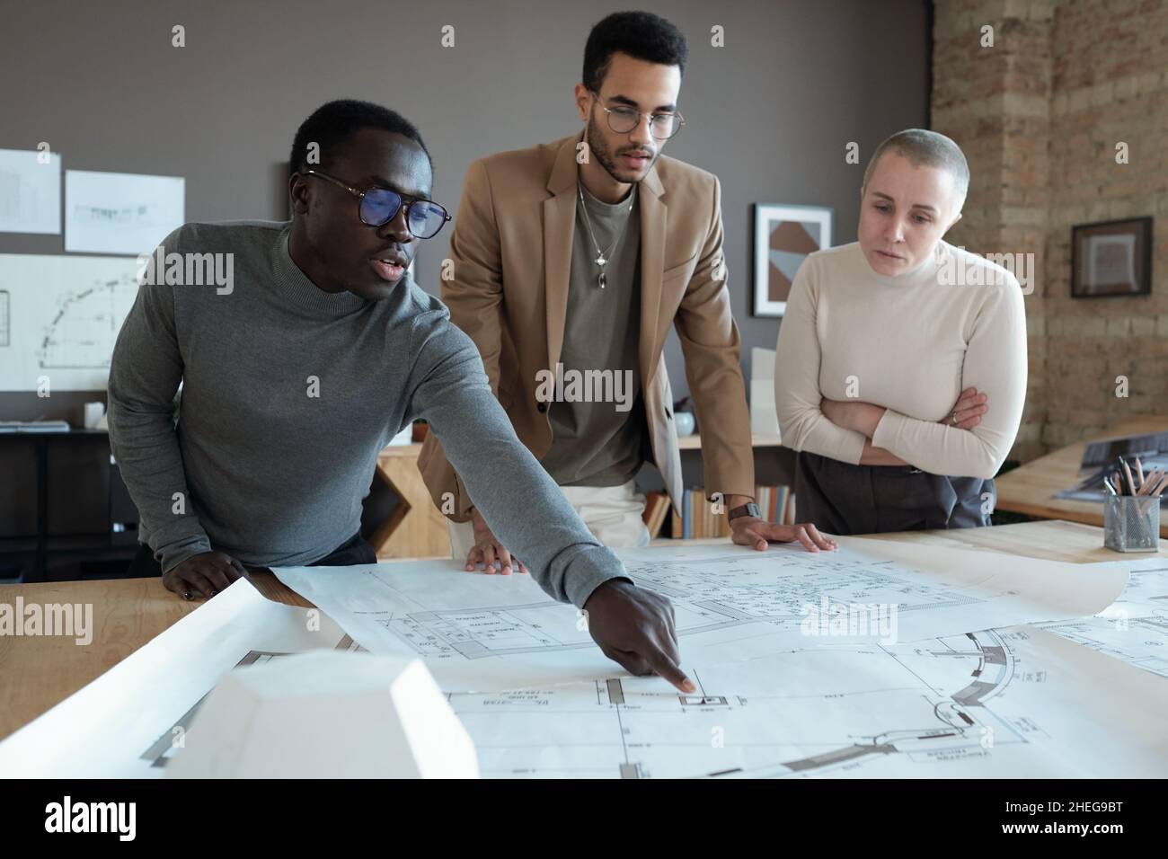 Young confident architect pointing at blueprint while bending over ...