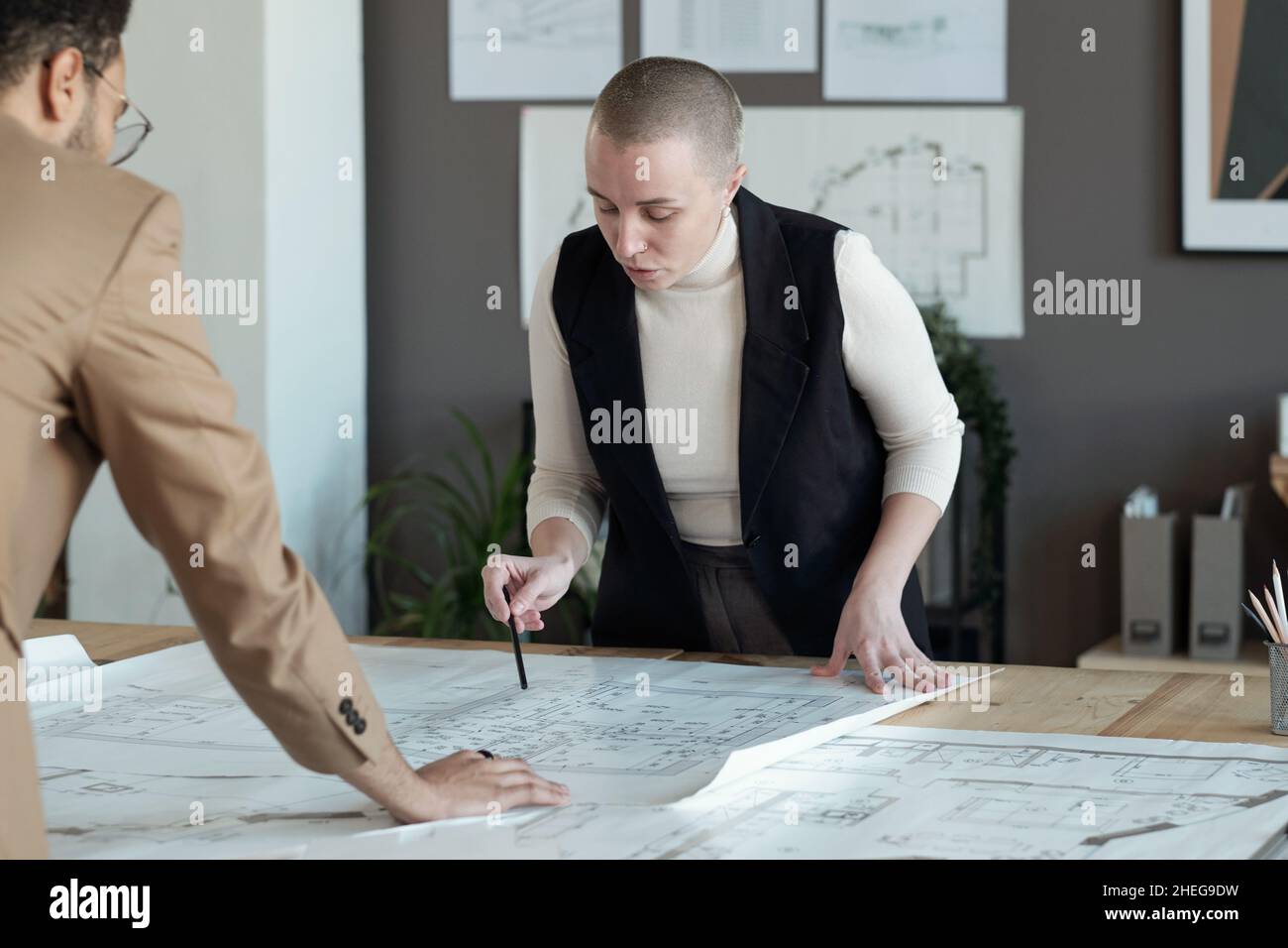 Confident businesswoman bending over table with blueprint while ...