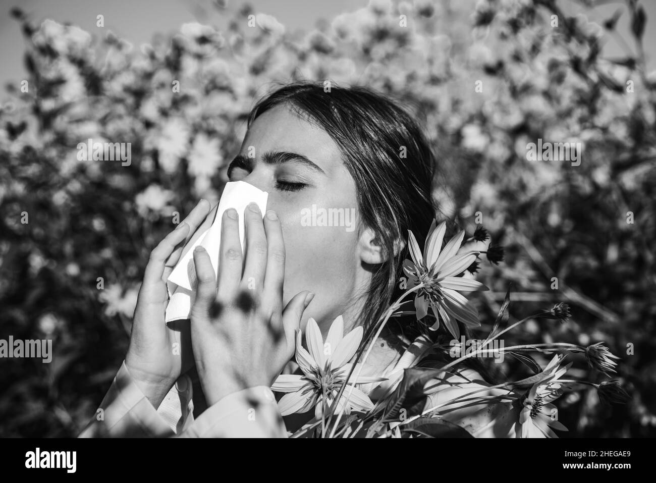 Young girl sneezing and holding paper tissue in one hand and flower ...