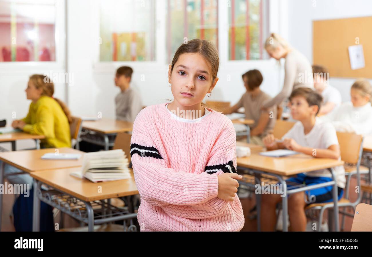 Upset girl stands in a school class against background of classmates ...