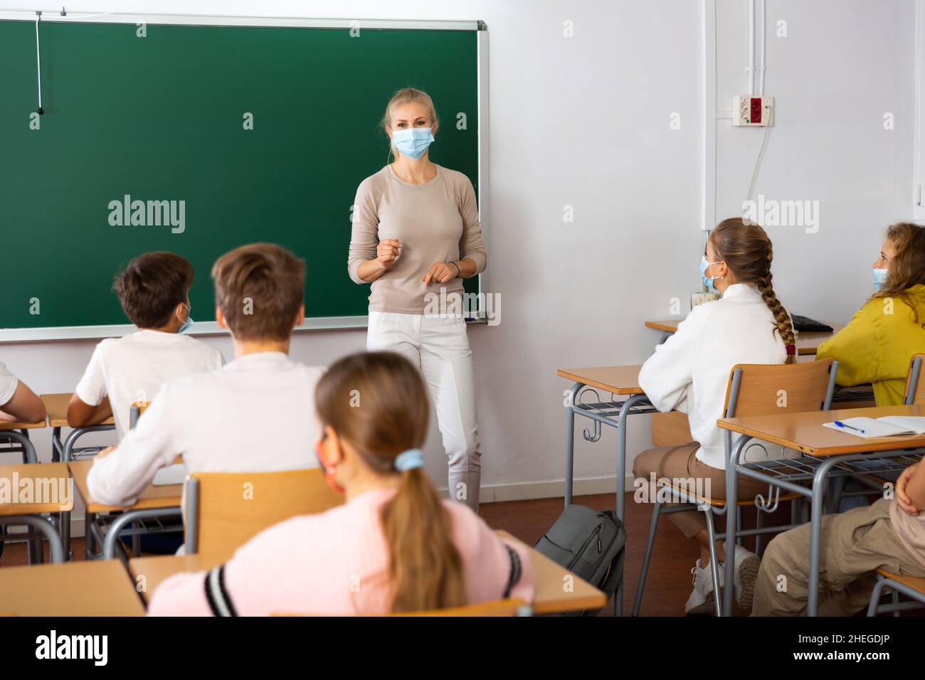 Teacher in mask explaining new theme to children Stock Photo - Alamy