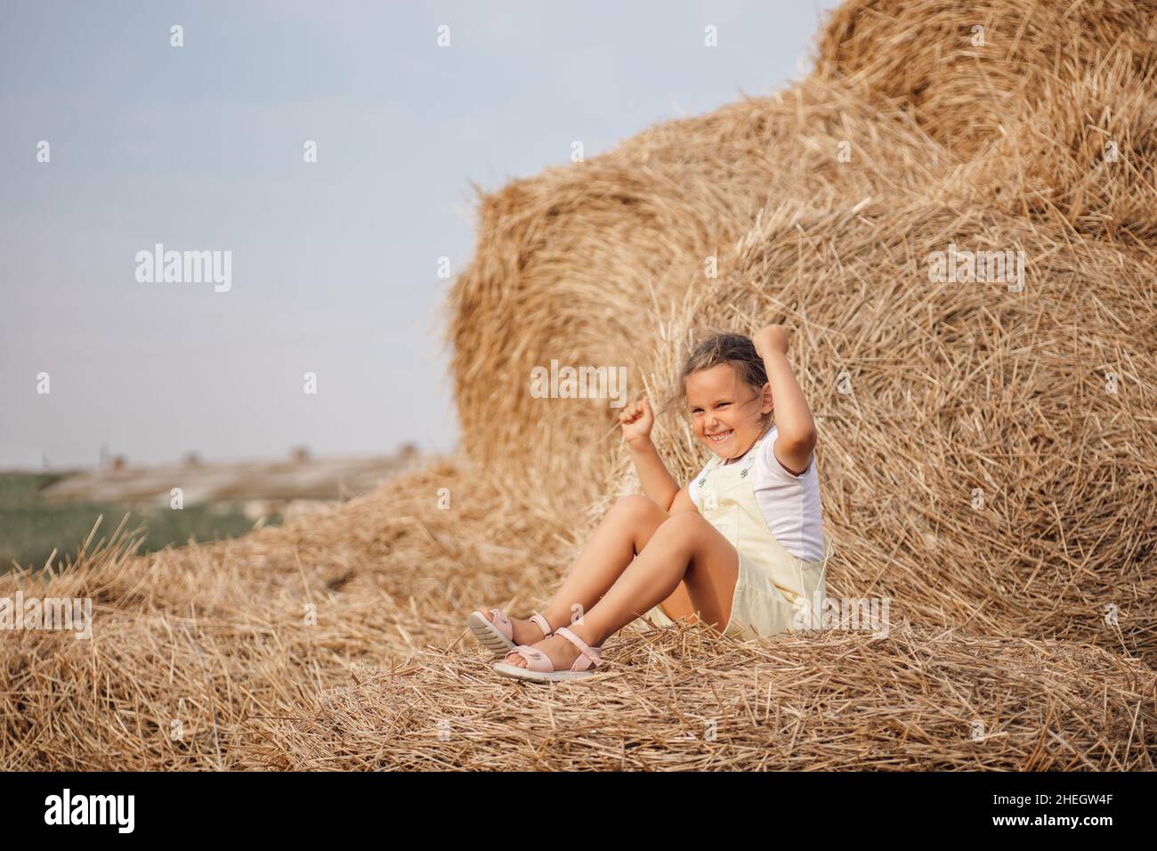 Portrait of young Caucasian little girl having fun sitting on haystacks ...