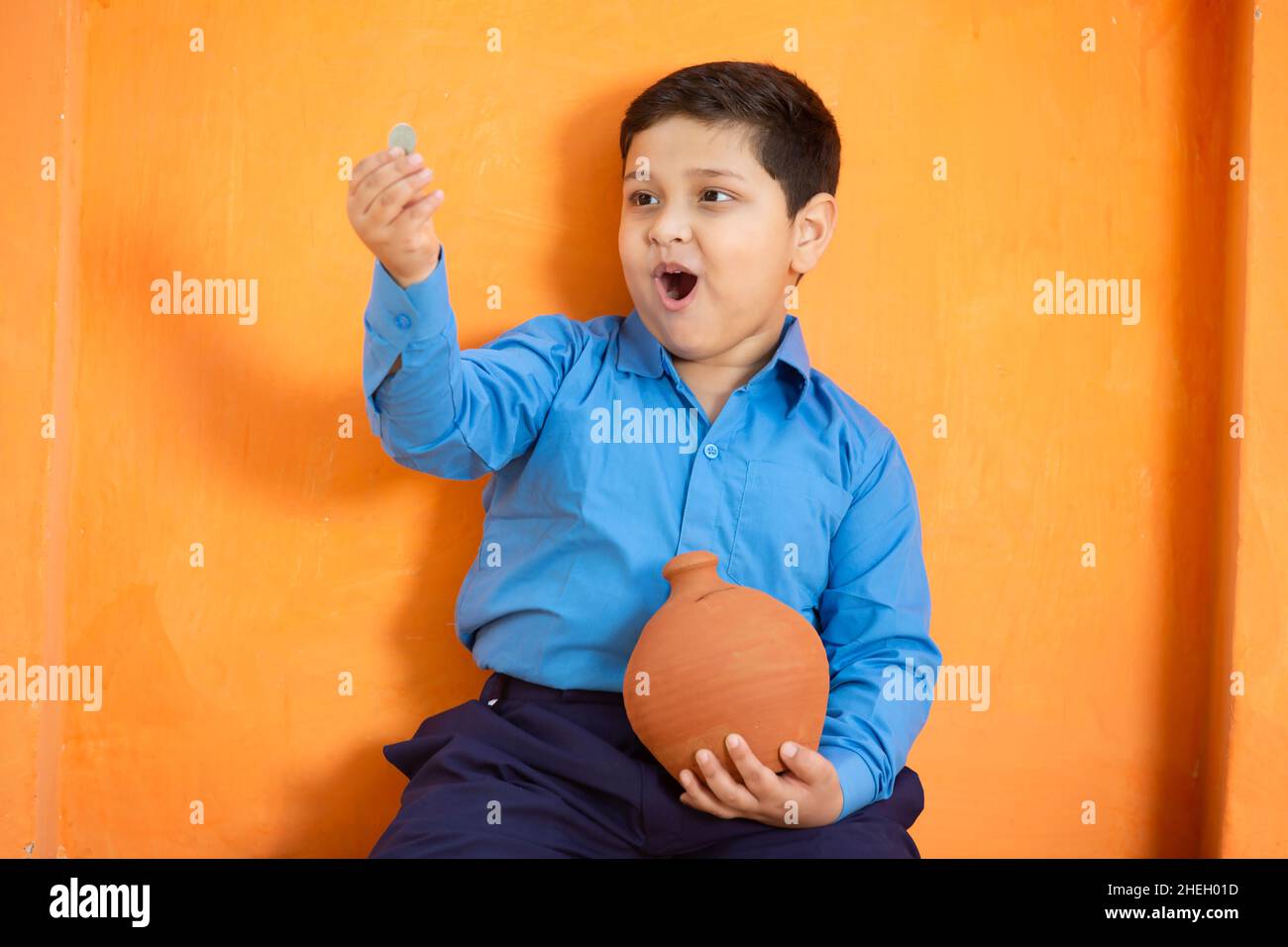 Happy cute little Indian boy holding coin in hand and clay money box or ...