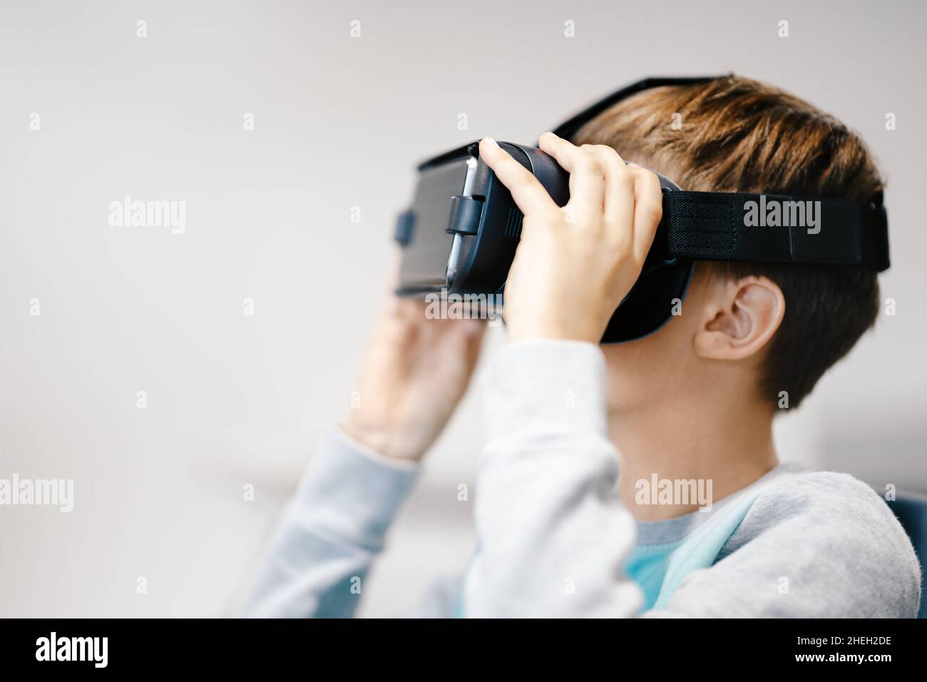 Amazed child with virtual reality headset sitting behind table indoors ...