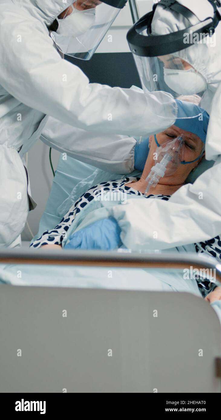 Medical team with protective uniforms using oxygen tube on sick patient ...