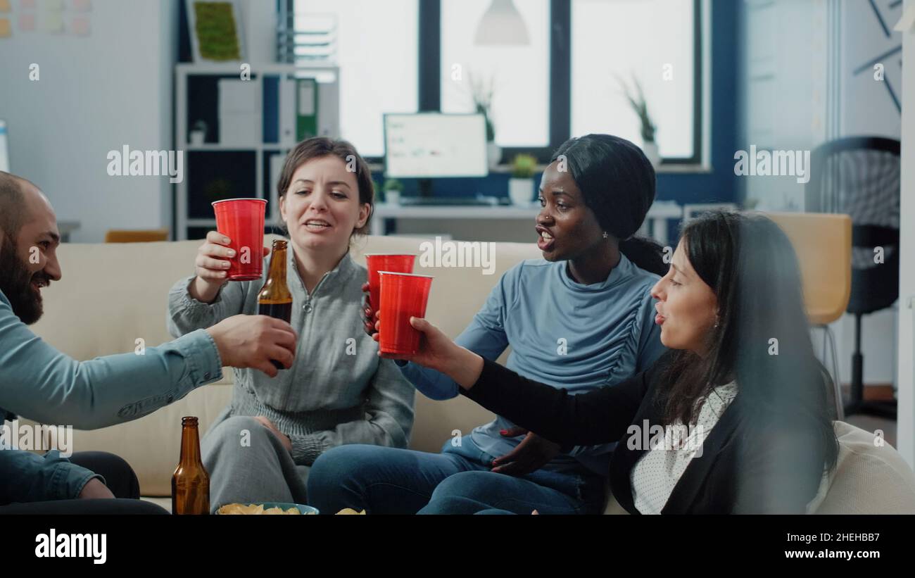 Cheerful coworkers cheers with cups and bottles of beer after work at ...