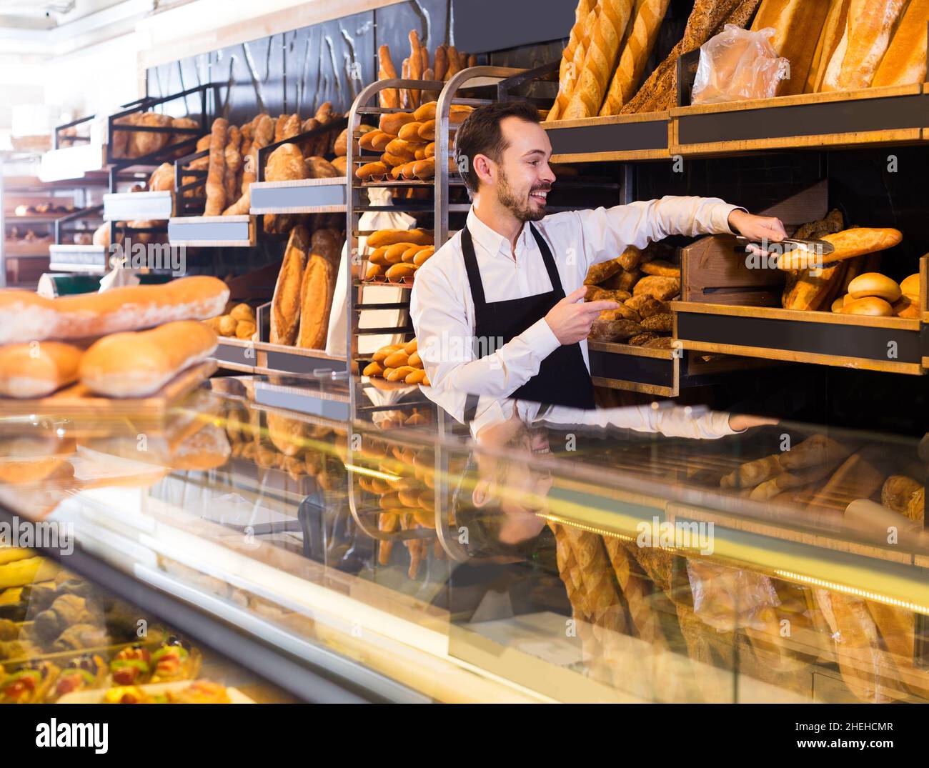 Male Shop Assistant Demonstrating Delicious Loaves Of Bread In Bakery