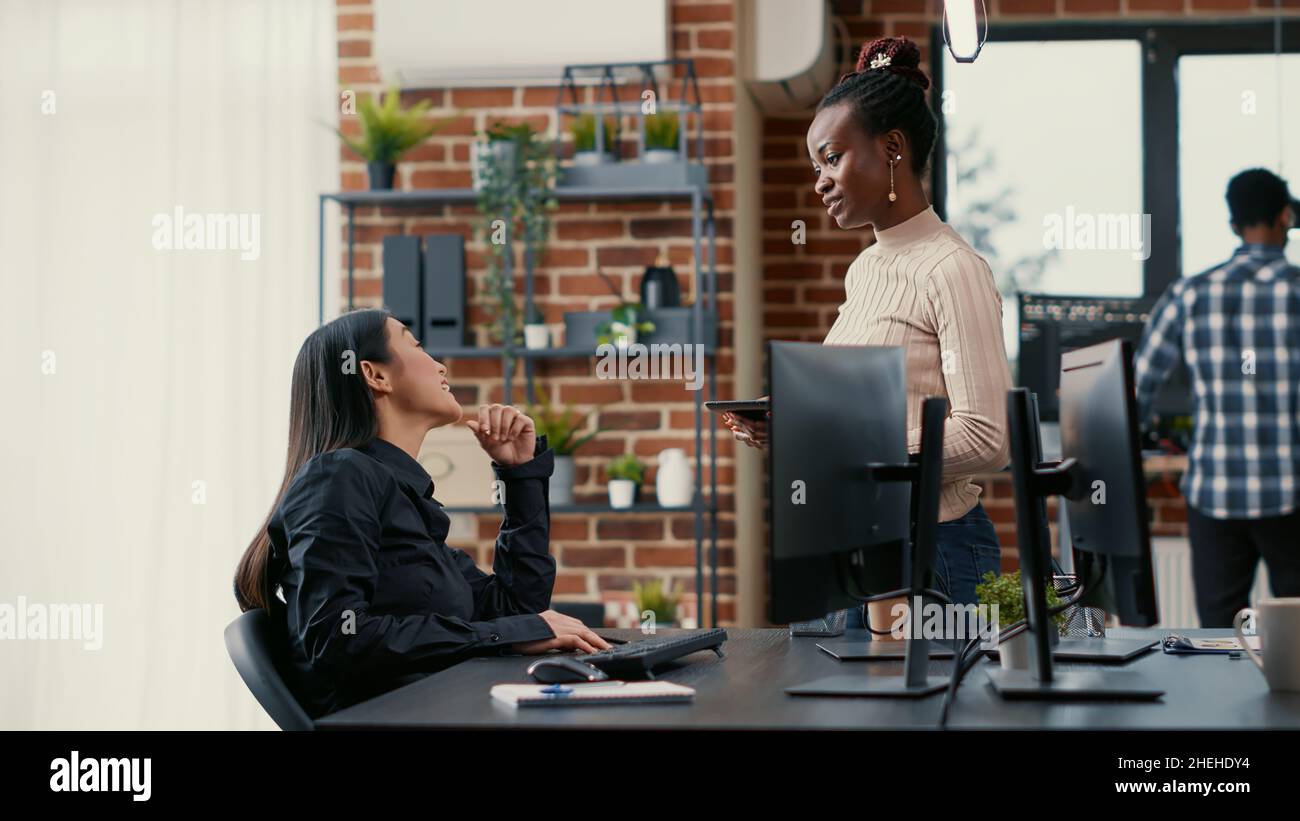 Programer standing up holding digital tablet talking with coder sitting ...