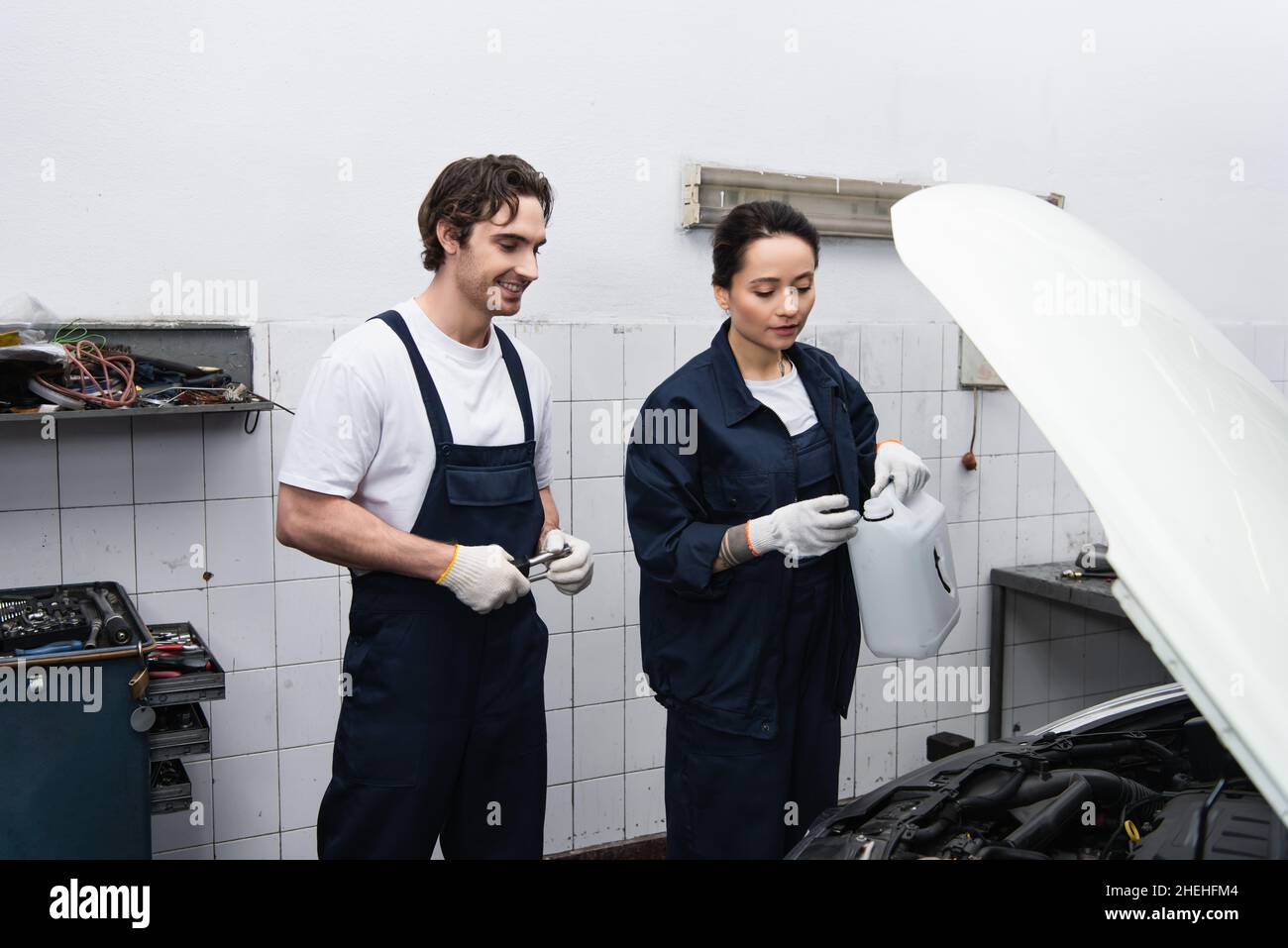 Mechanic holding canister near smiling colleague and car in garage ...