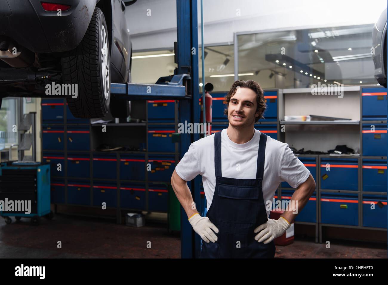 Smiling mechanic holding hands on hips in garage Stock Photo - Alamy