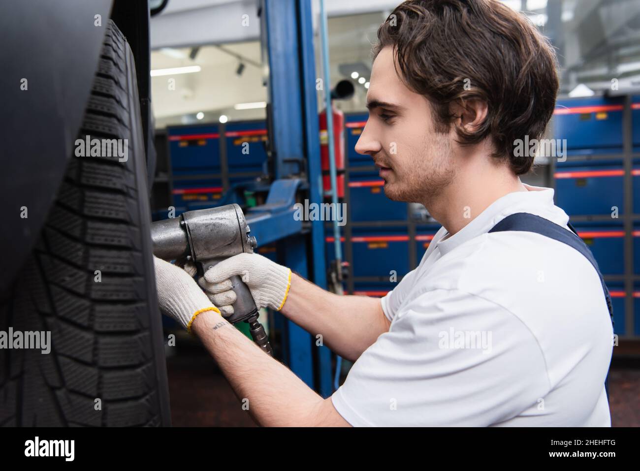 Side view of mechanic working with impact wrench on car wheel in garage ...