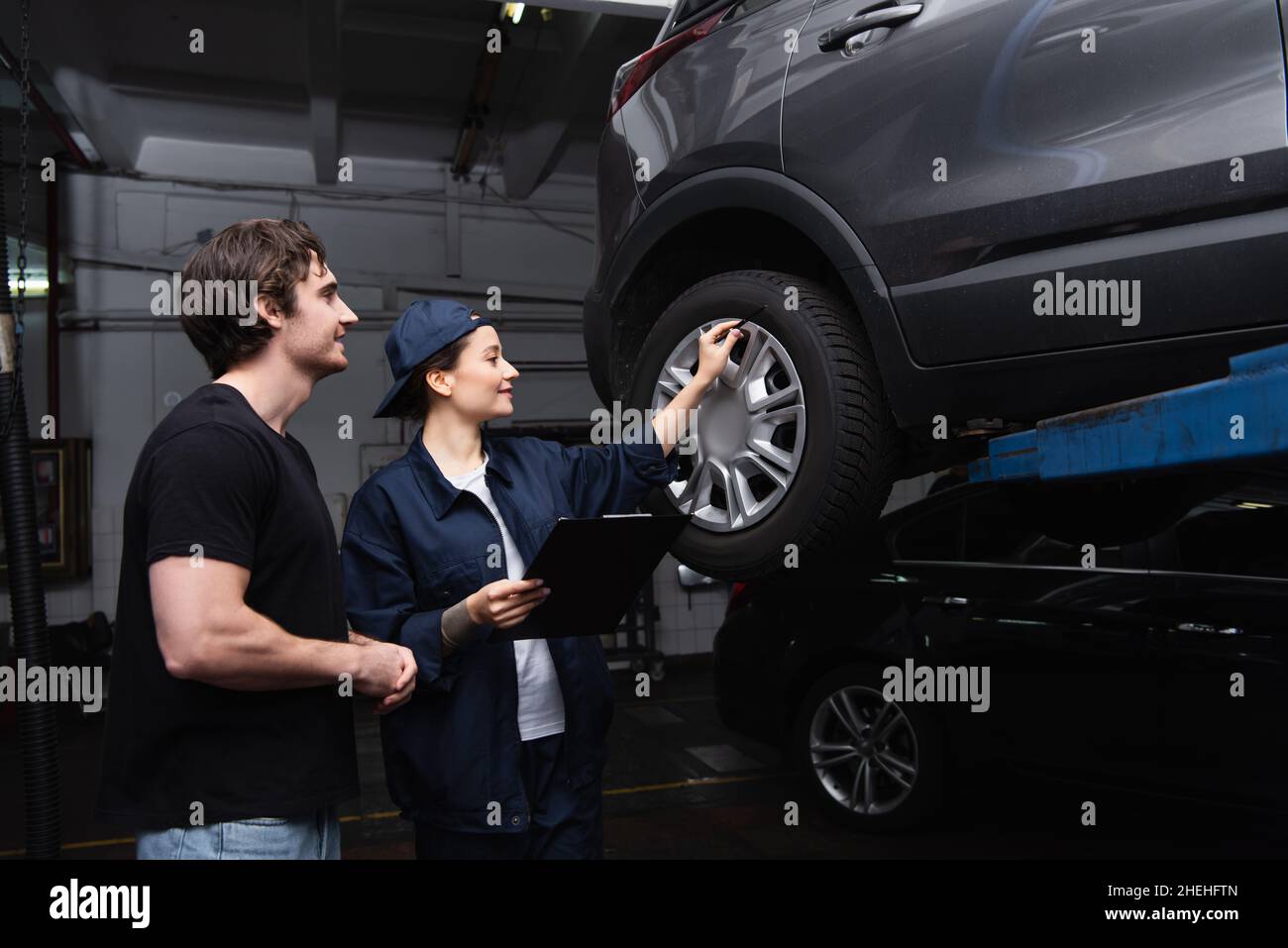 Side view of forewoman with clipboard pointing at car wheel near driver ...