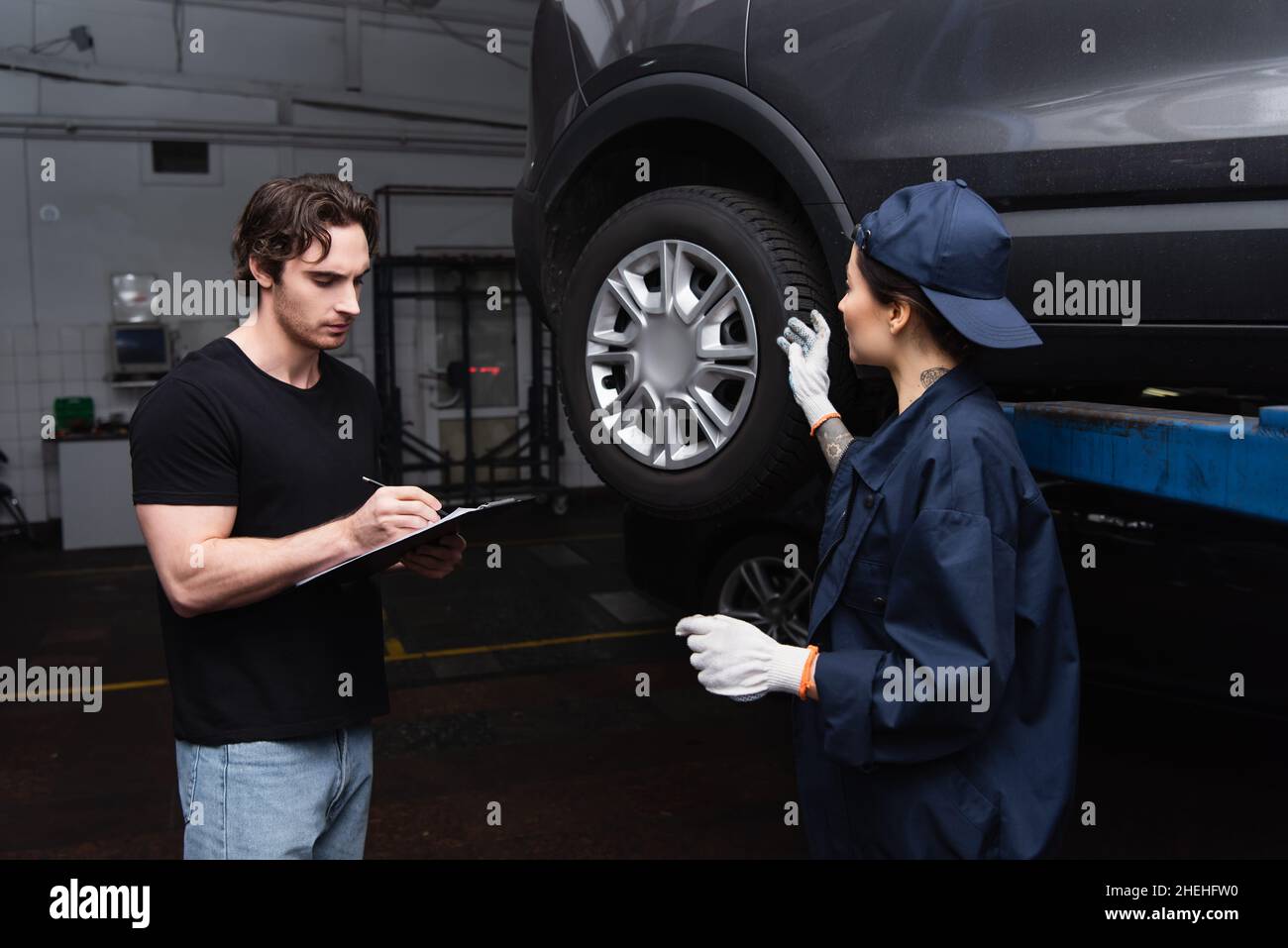Mechanic pointing at car wheel near colleague writing on clipboard in ...