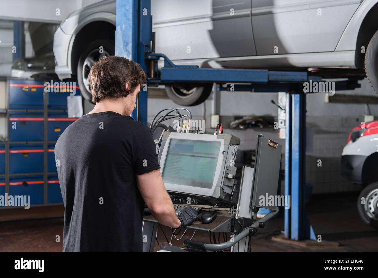 Workman using computer near auto in garage Stock Photo - Alamy