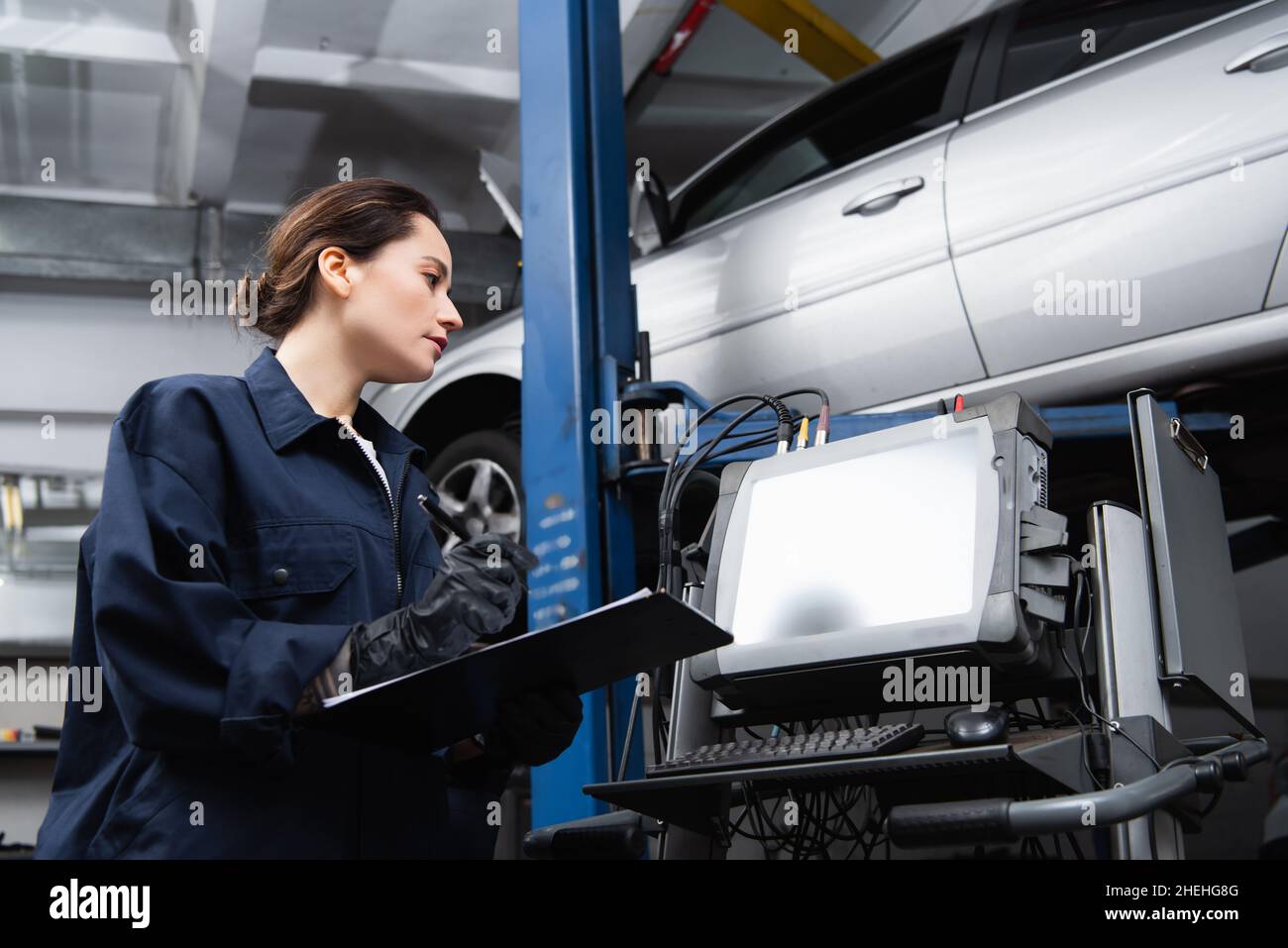 Side view of forewoman writing on clipboard near computer and car in ...