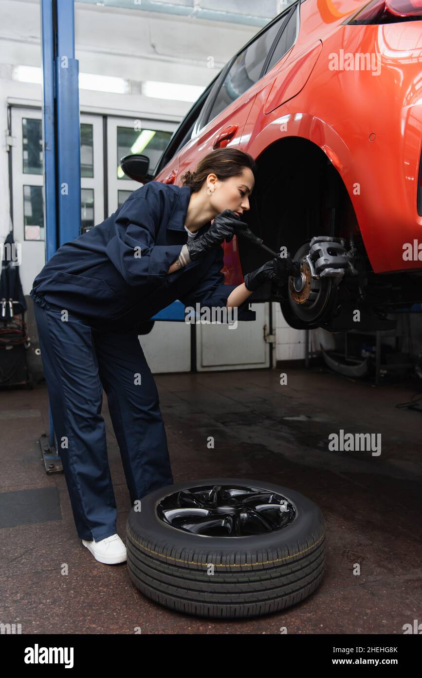 Side view of mechanic working with screwdriver and car wheel in garage ...