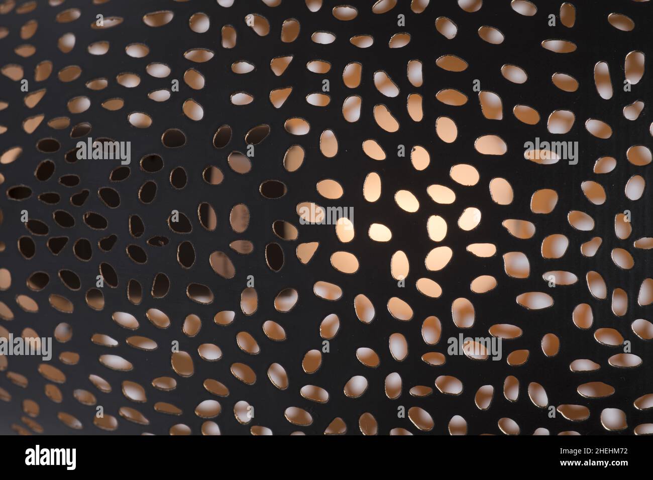 Close up of perforated dark sheet with yellow light source behind it as ...