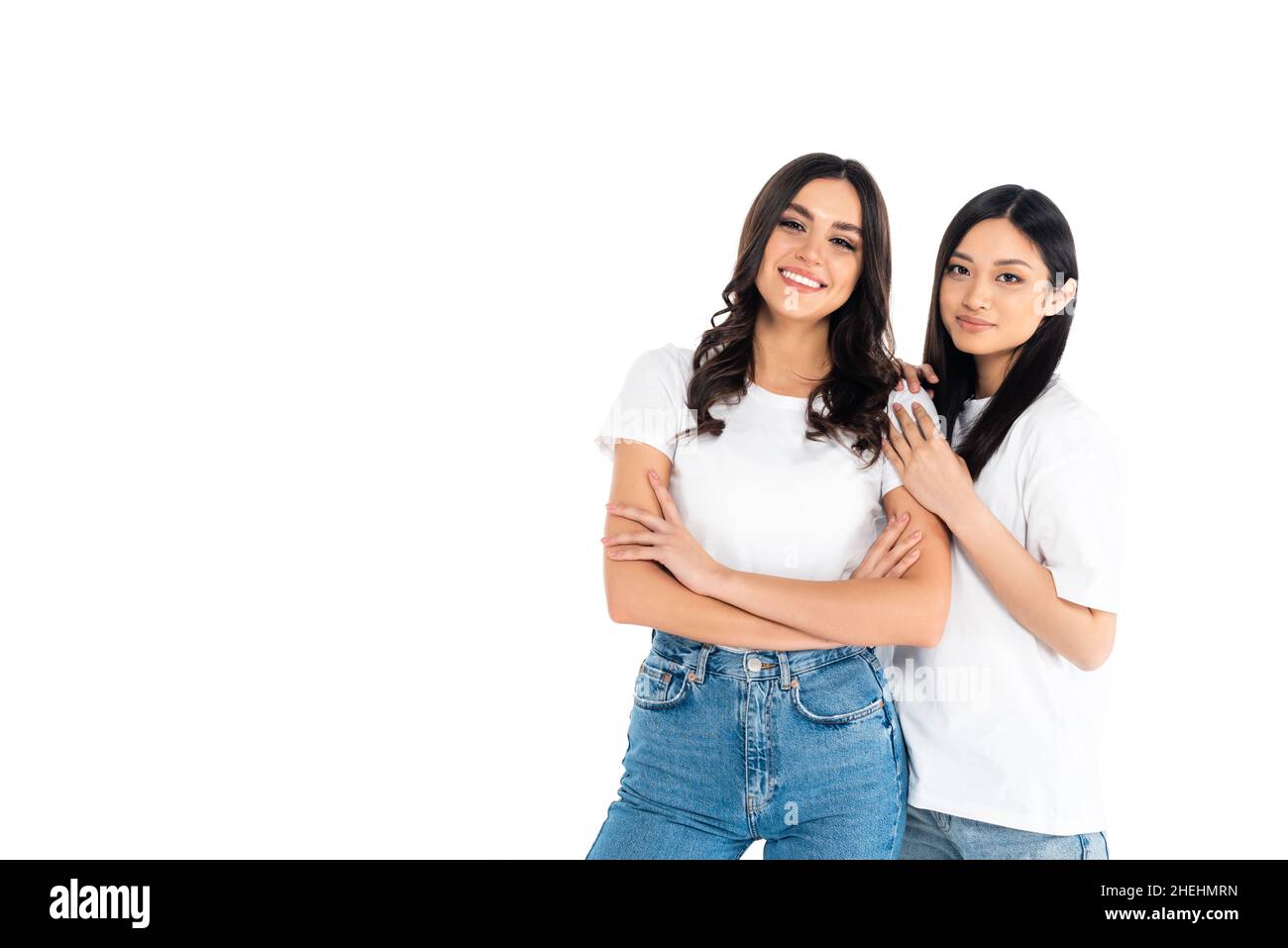 happy young woman standing with crossed arms near asian friend isolated ...