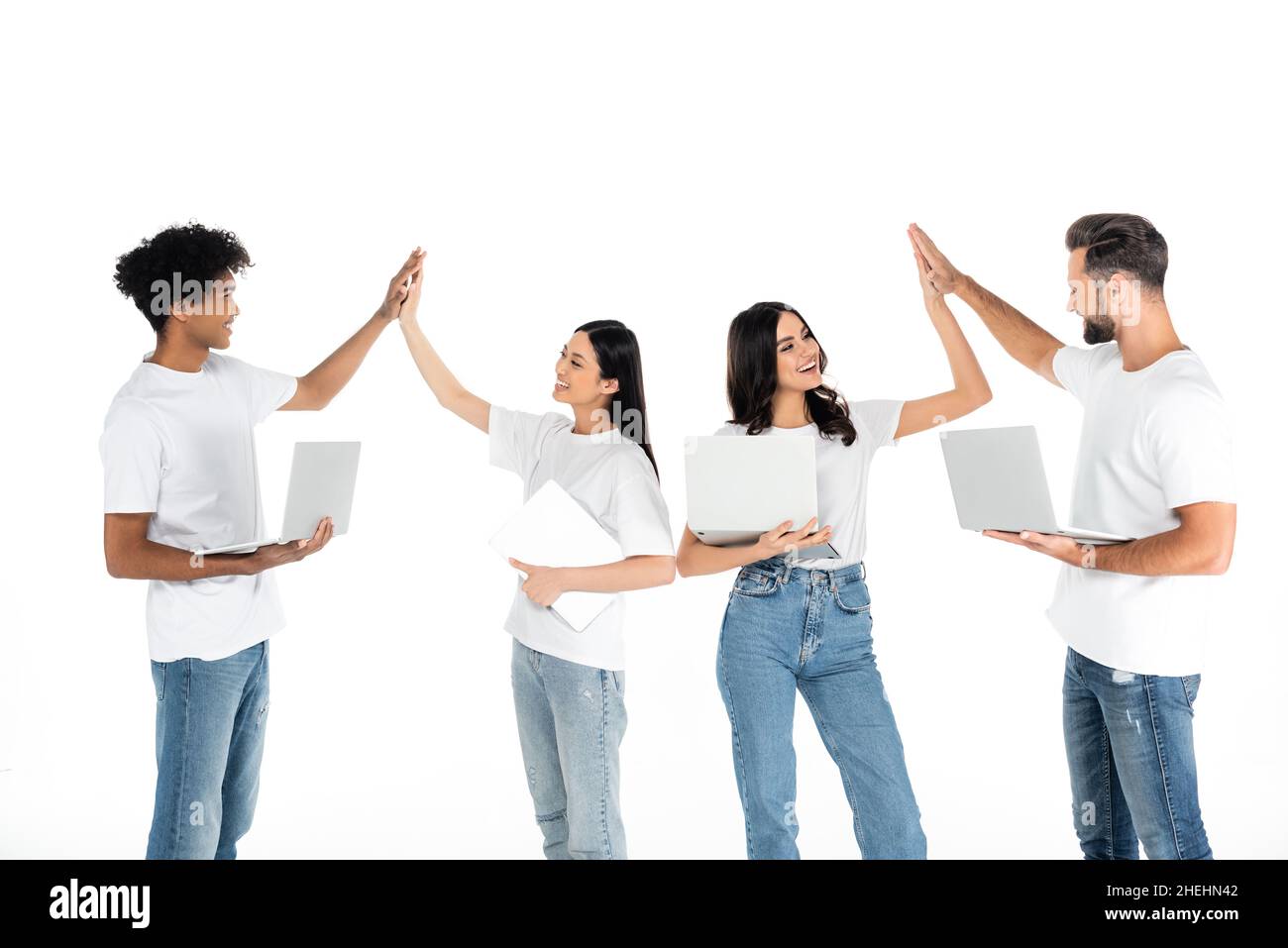 cheerful multicultural friends with laptops giving high five isolated ...