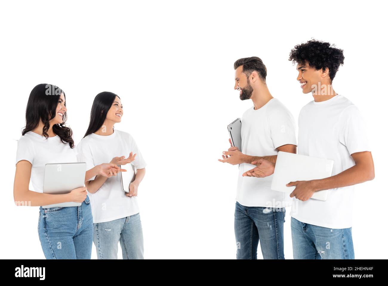 smiling multiethnic friends with laptops pointing at each other while ...