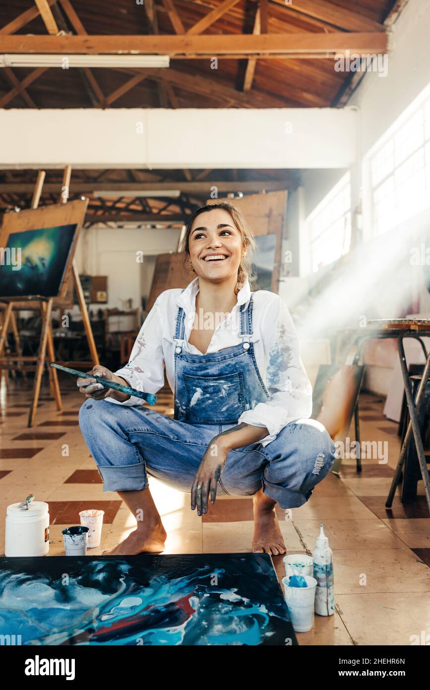 Inspired young artist looking away with a smile in her art studio ...