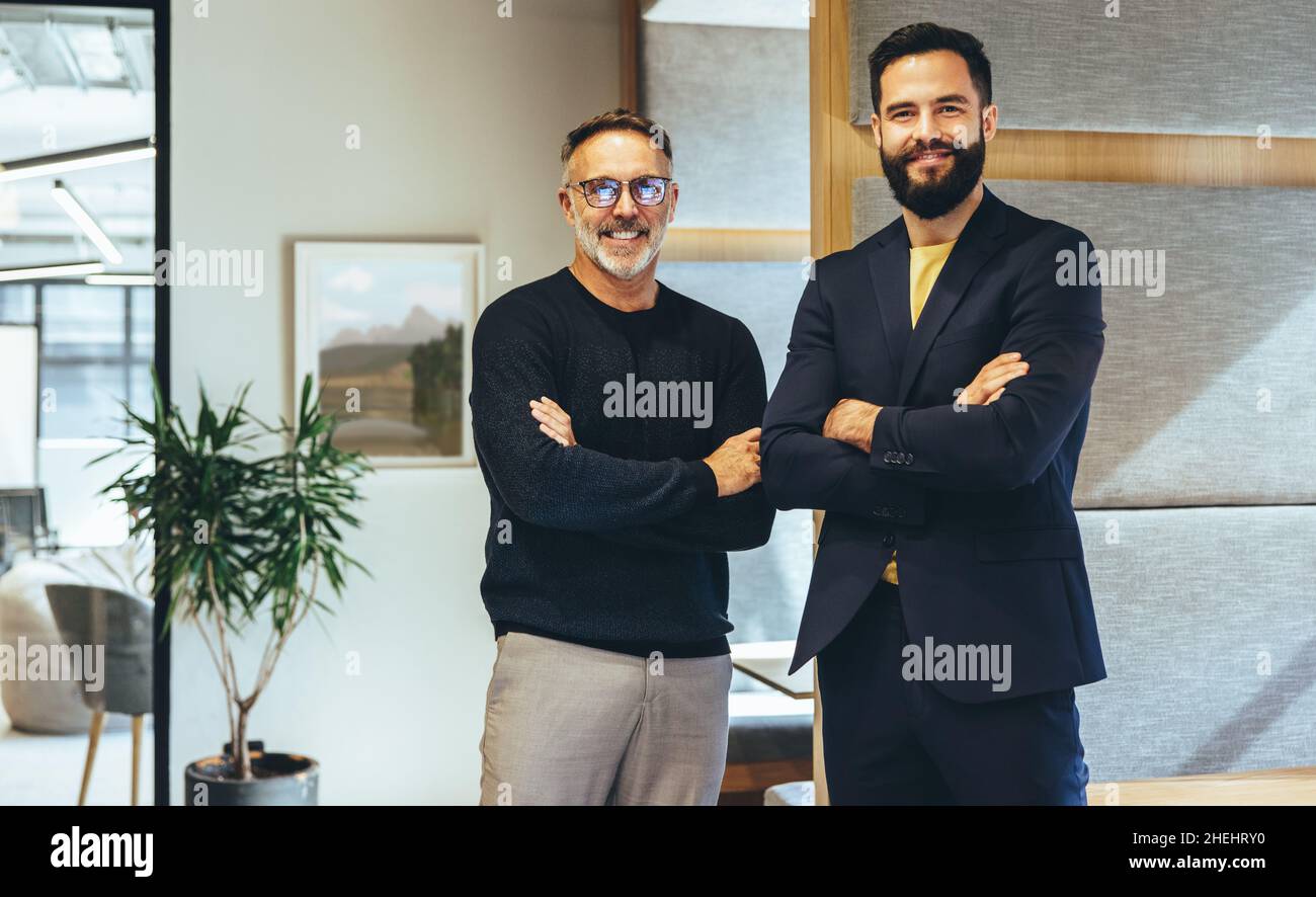 Two successful businessmen smiling at the camera while standing with ...