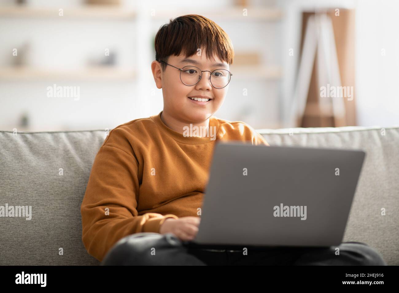 Cheerful chinese kid sitting on couch with laptop at home Stock Photo ...