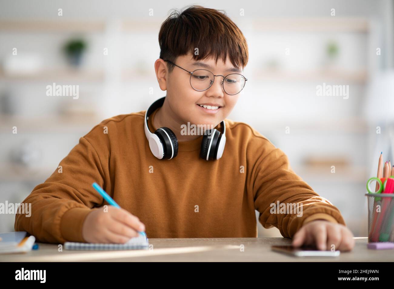 Smiling japanese kid with headset sitting at table, using smartphone ...
