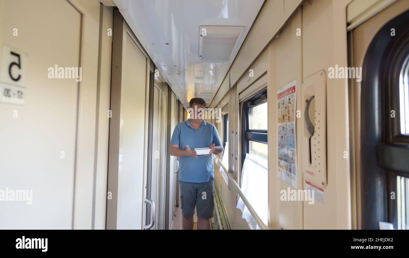 man slowly walks with hot instant noodles along corridor of a moving ...