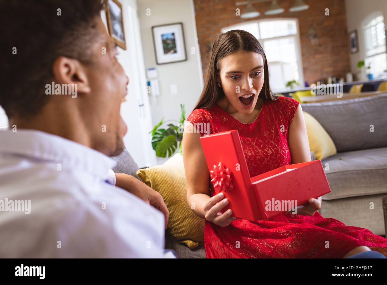 Surprised young biracial beautiful woman opening gift box by excited ...