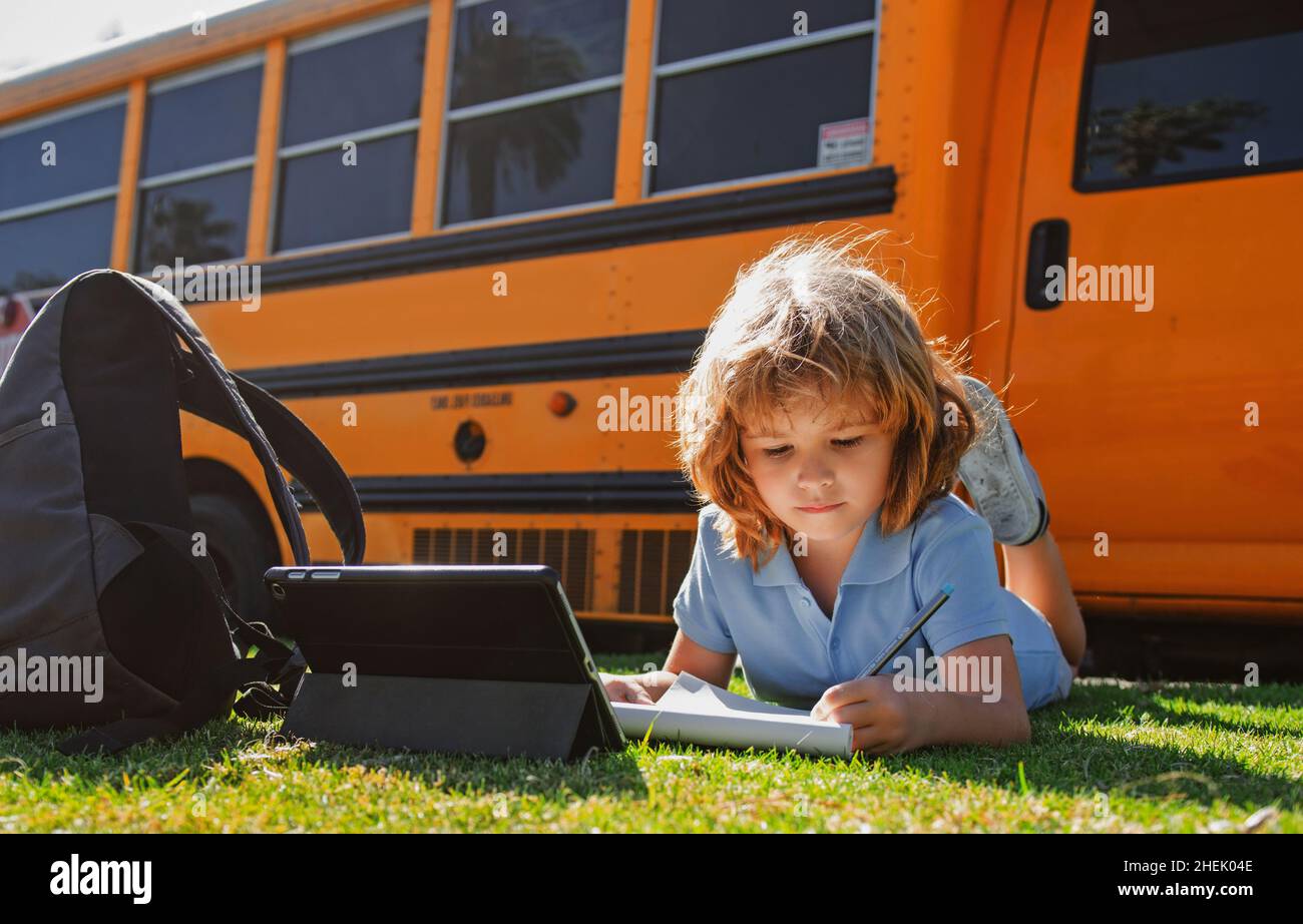 Smart schoolboy on laying on grass with digital tablet at school park ...