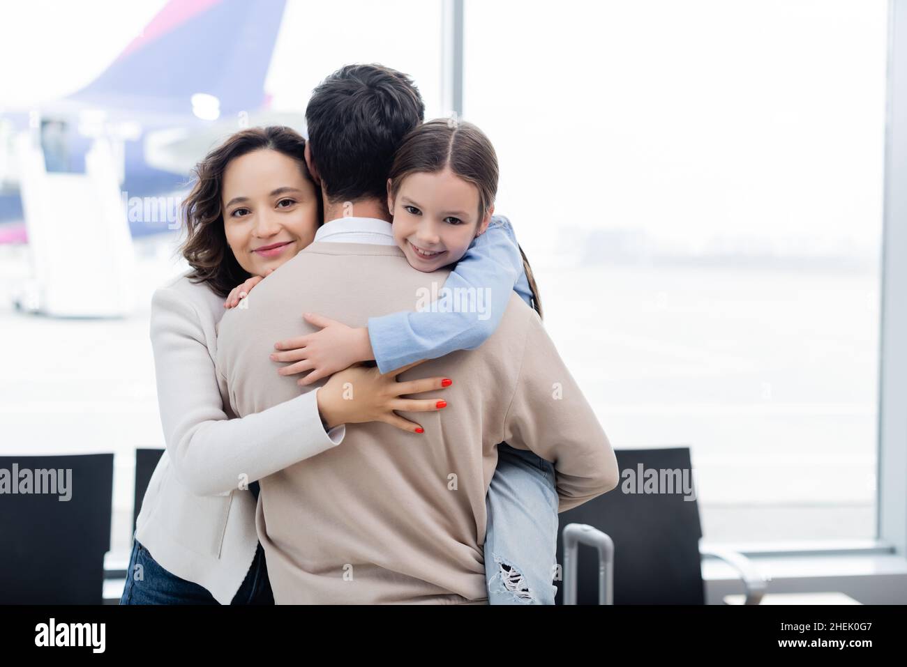 cheerful woman and kid hugging man in airport Stock Photo - Alamy