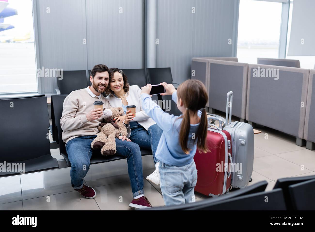 kid taking photo of happy parents with paper cups in airport lounge ...
