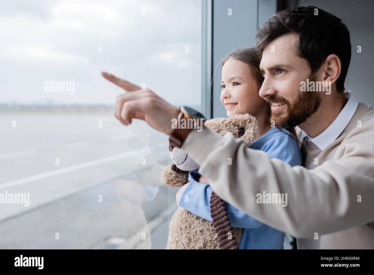 happy man pointing with finger at window near daughter with soft toy in ...
