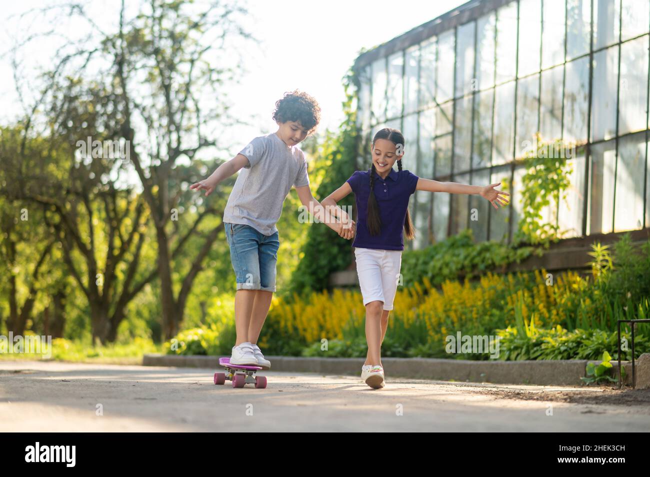 Boy learning to ride the skateboard aided by a girl Stock Photo - Alamy