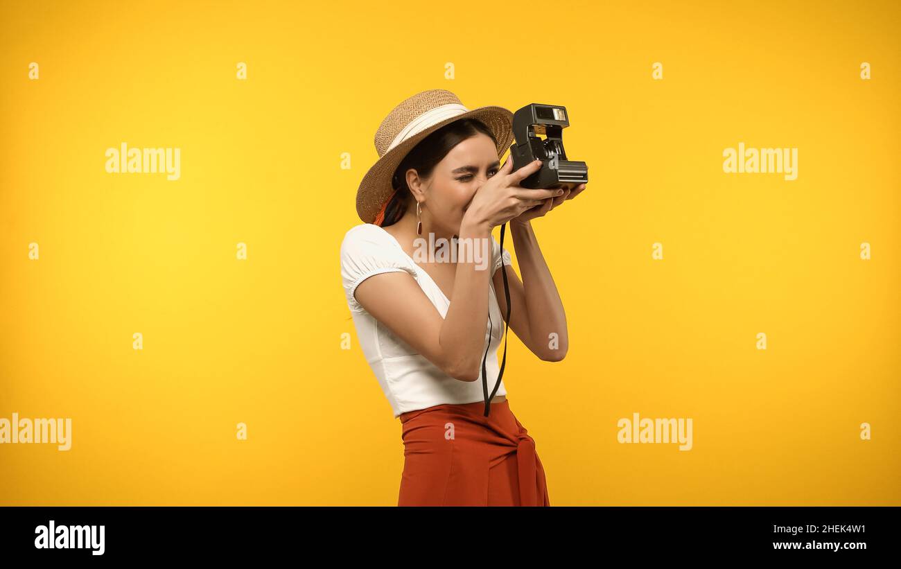 Woman in straw hat taking photo on vintage camera isolated on yellow ...
