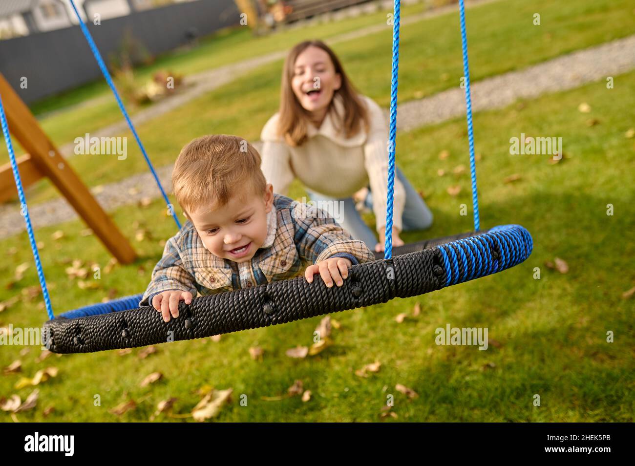 Woman pushing swing with joyful child Stock Photo - Alamy