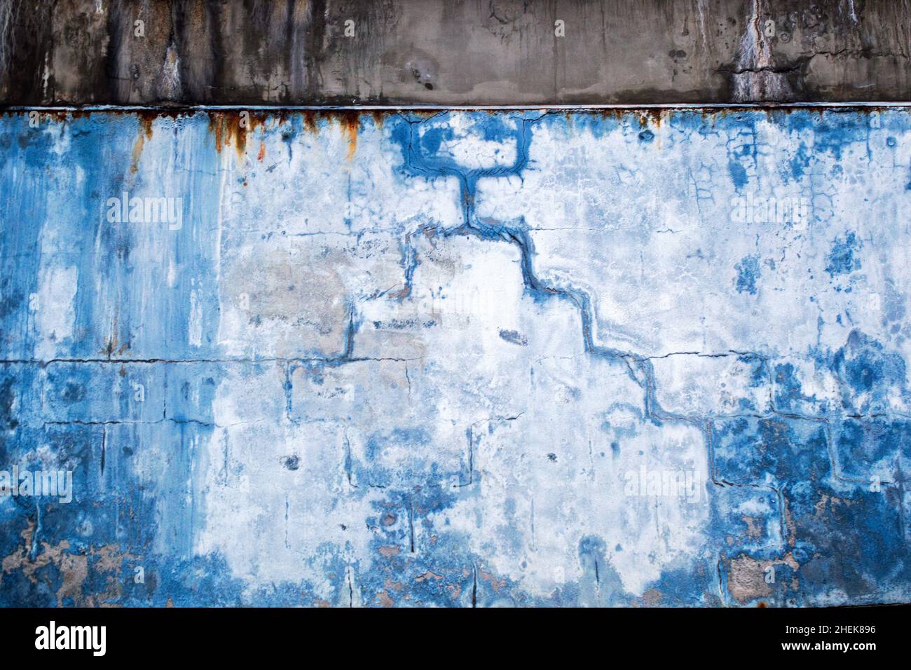 Blue painted wall with different shades of flaked paint and cracks in ...