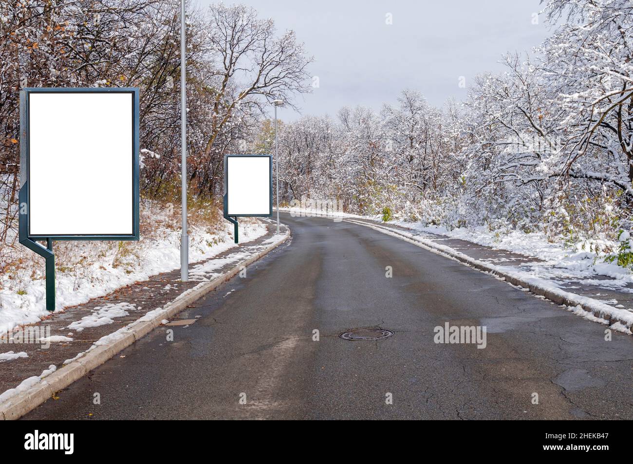 Two billboards on country asphalt road with tree covered with snow an ...