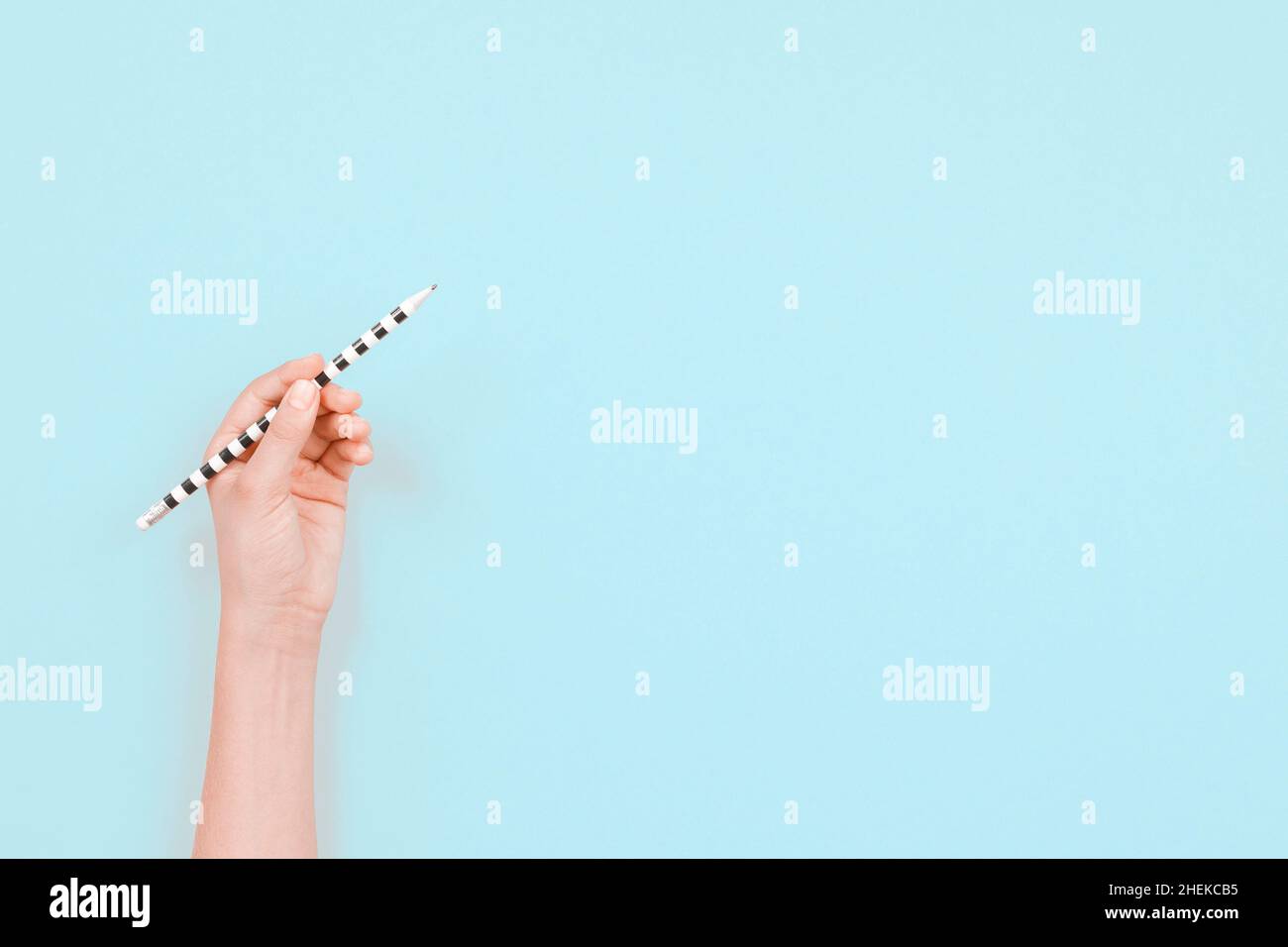Left hand holding pencil for writing over light blue background. Top ...