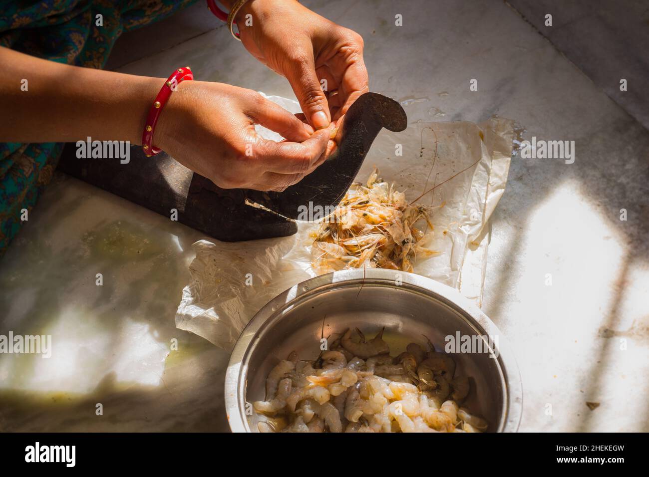 indian woman cutting or dressing raw shrimp for cooking in desi cutter ...