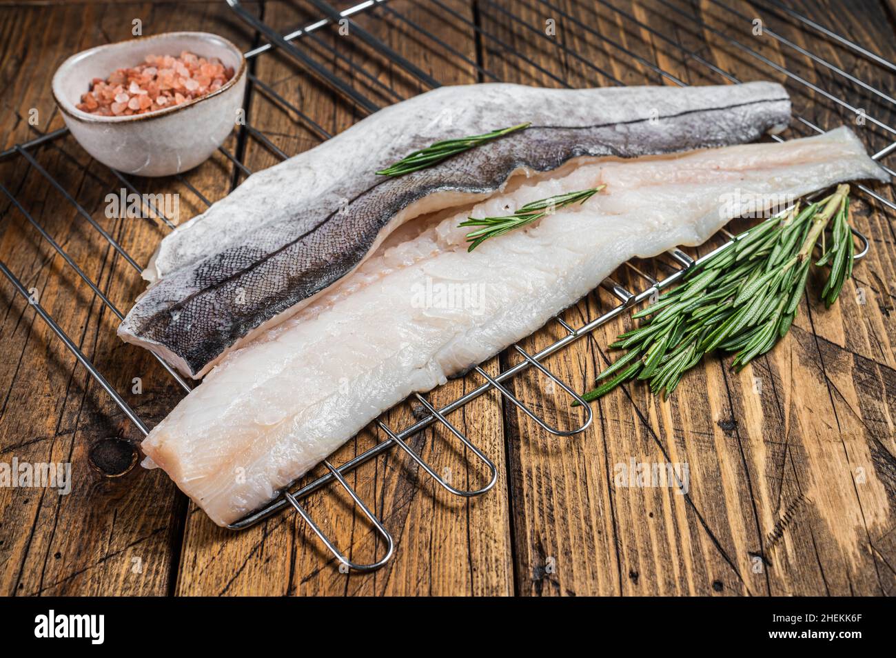 Raw fish fillets on grill with rosemary and herbs. Wooden background ...