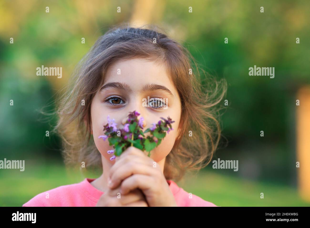 Little cute girl with pinc flowers. Child playing in summer garden ...