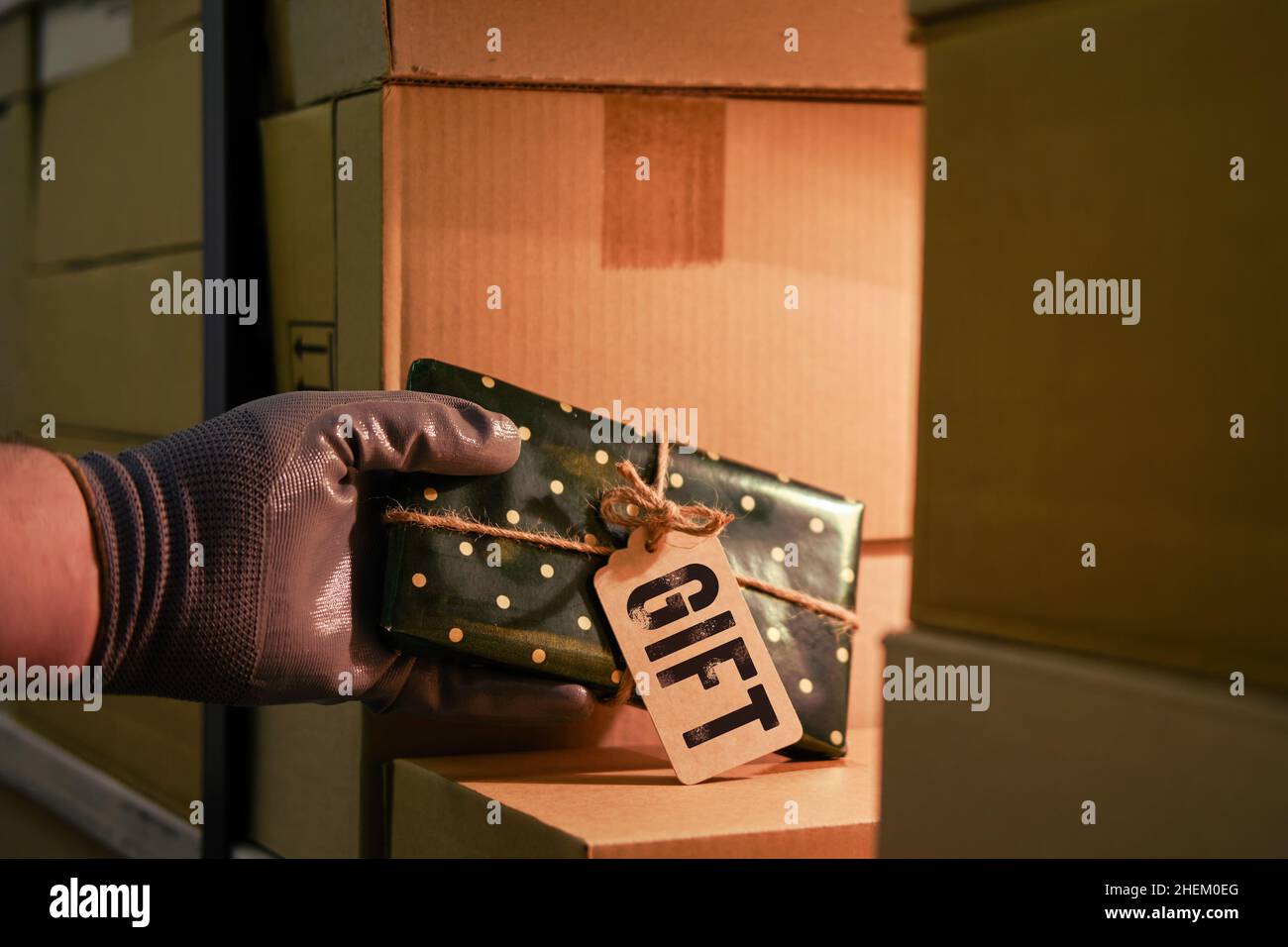 Man gloved hand holds a packed gift in a warehouse with boxes for ...